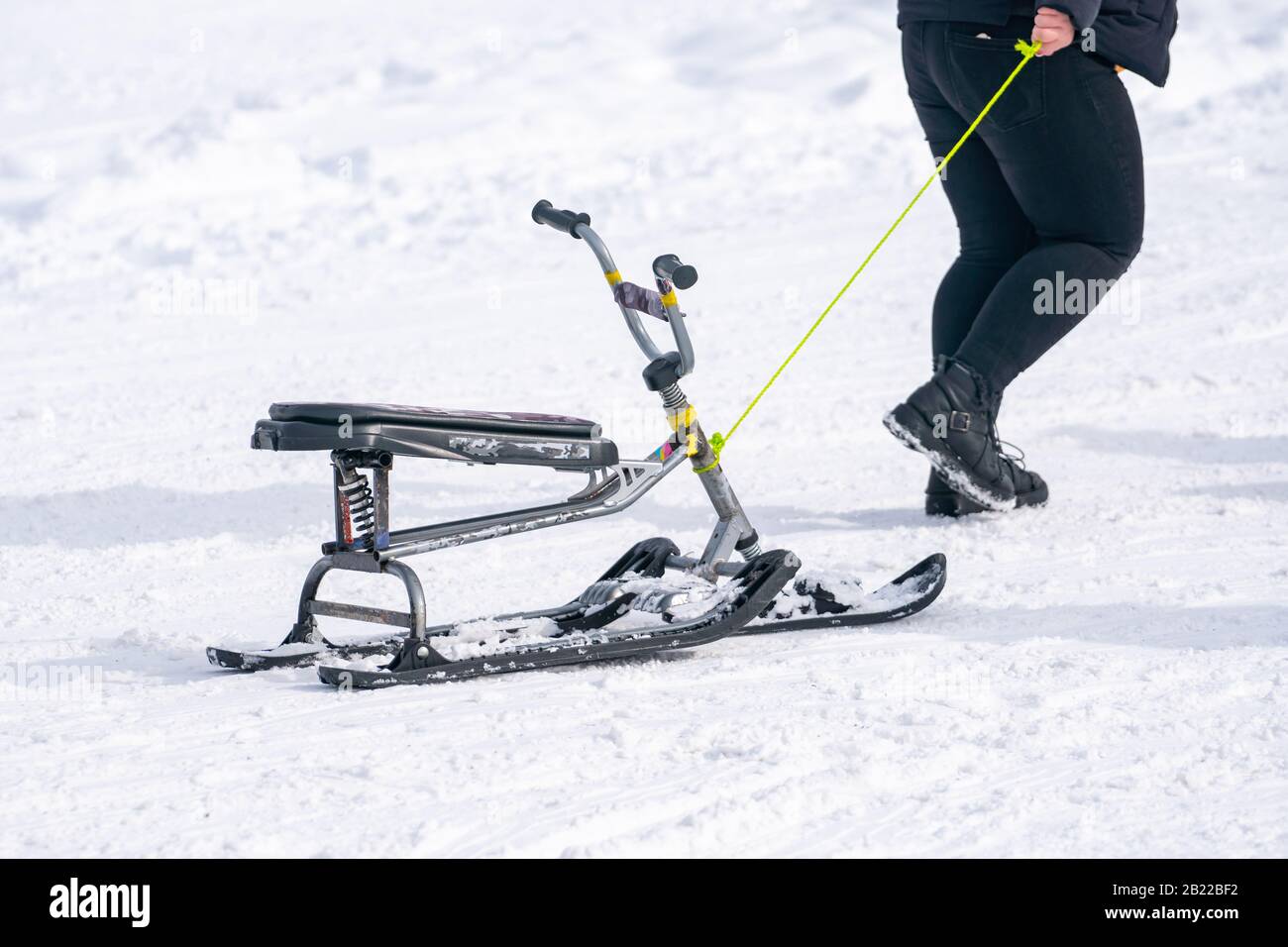 Back view of child in pulling sledge and running up snowy slope while ...