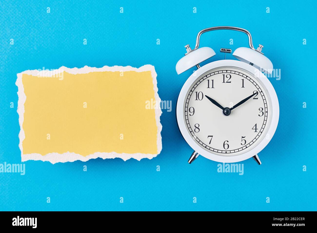 White alarm clock and empty torn paper sheet on blue background, top ...