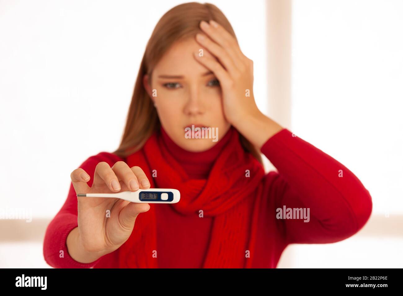 Beautiful young woman checks fever with thermometer as she feels ill ...