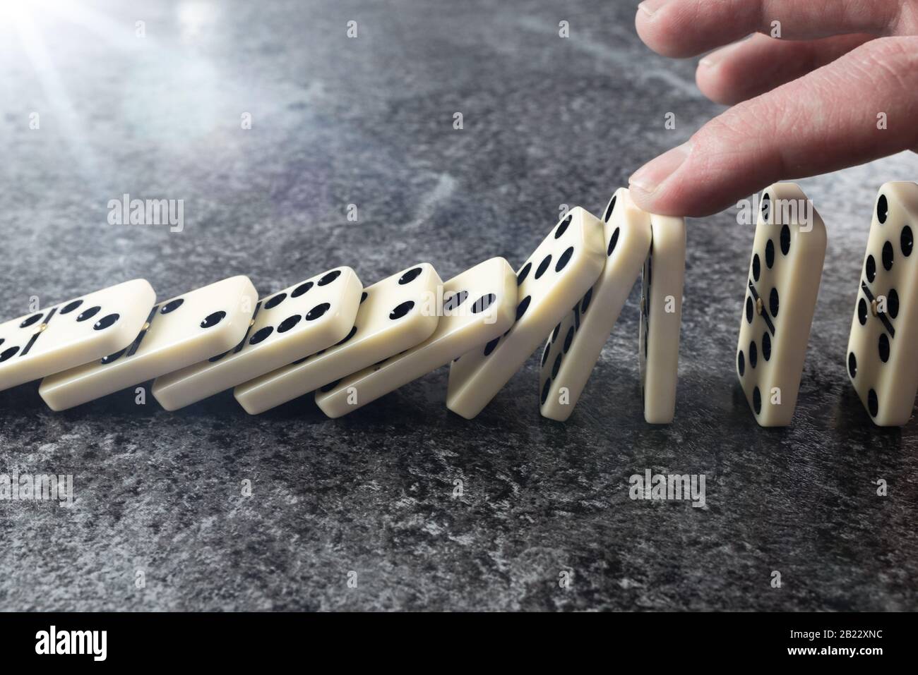 close-up of male hand preventing line of domino tiles from toppling and ...