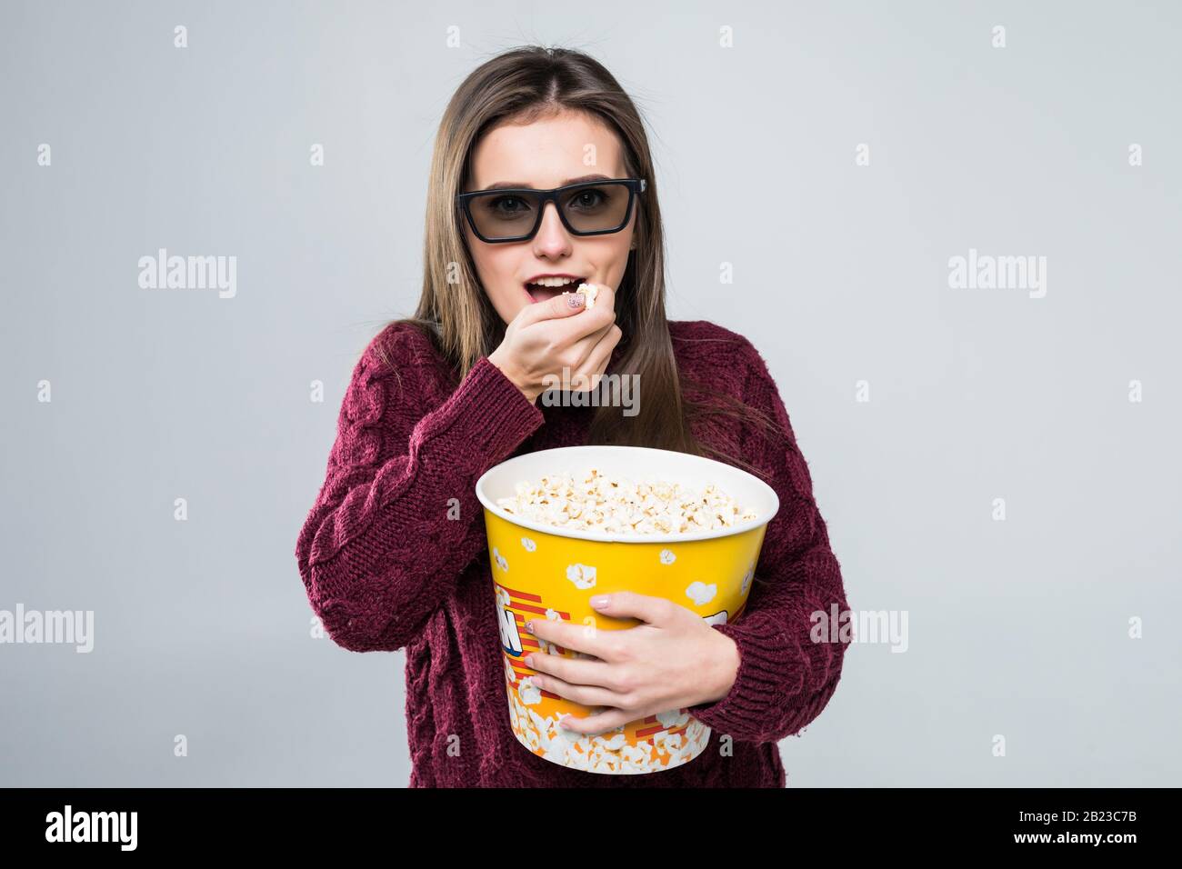 Girl in 3D glasses drinking beverage with bowl of popcorn and watching cinema, isolated on white ...