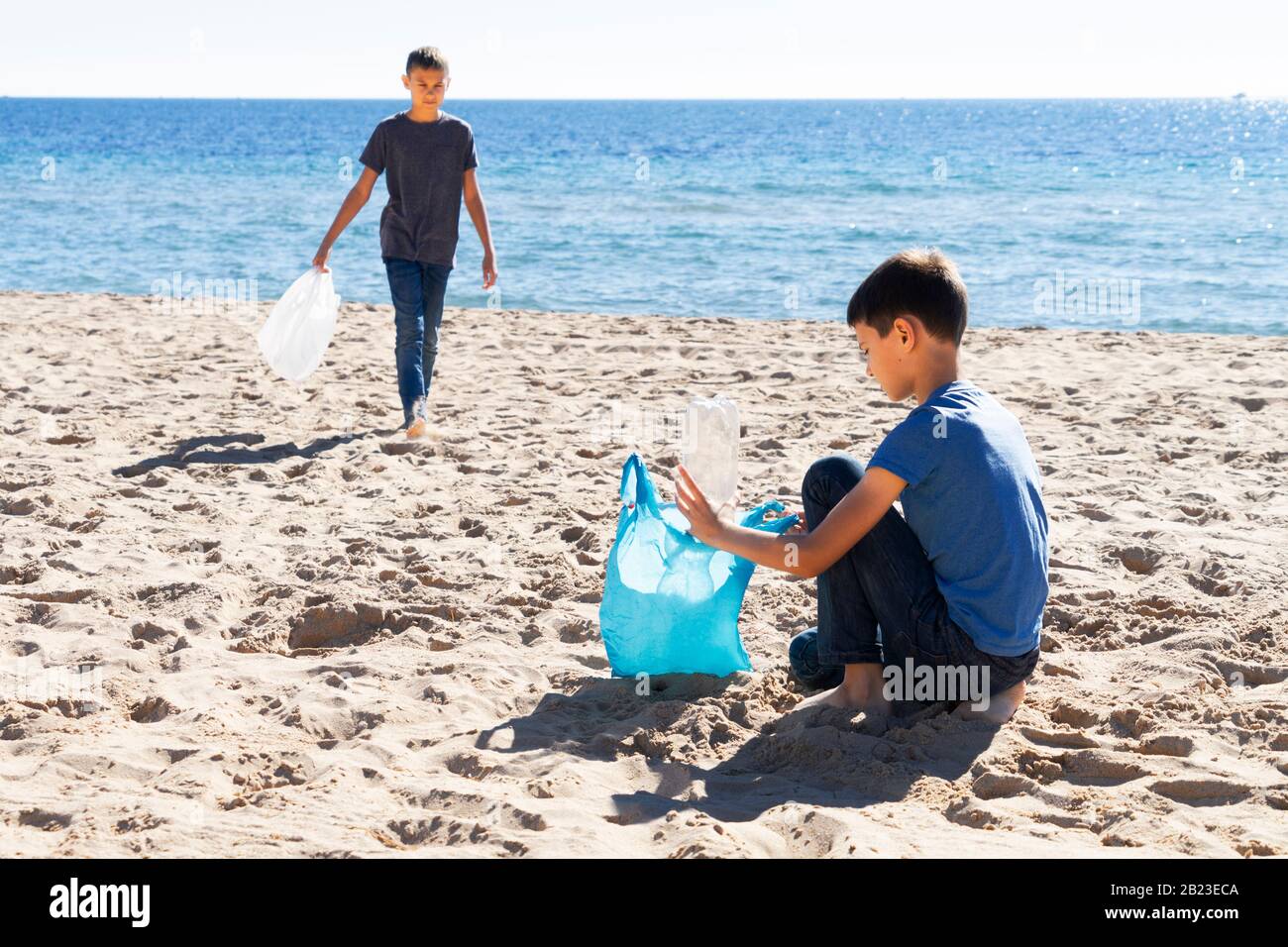 Volunteers cleaning beach from plastic. Boys walking on the beach and ...