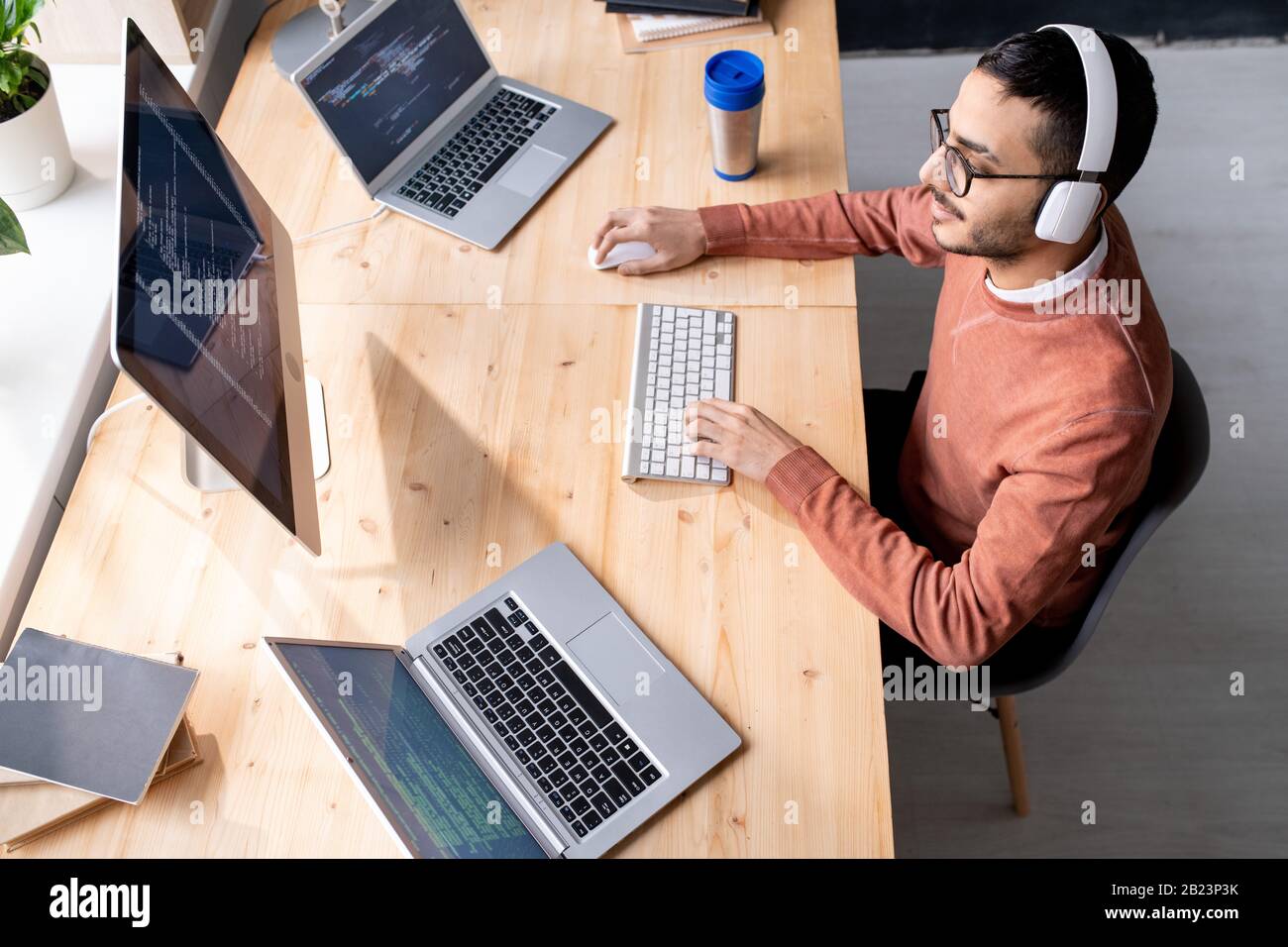 Busy young software developer in headphones sitting by table in front ...