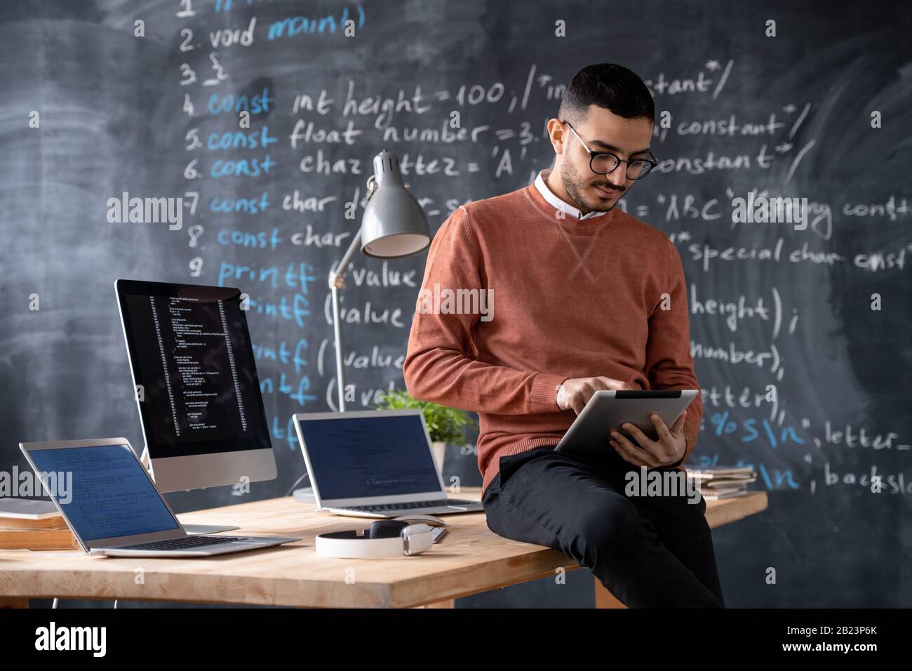 Clever young manager using touchpad while sitting on table with two ...