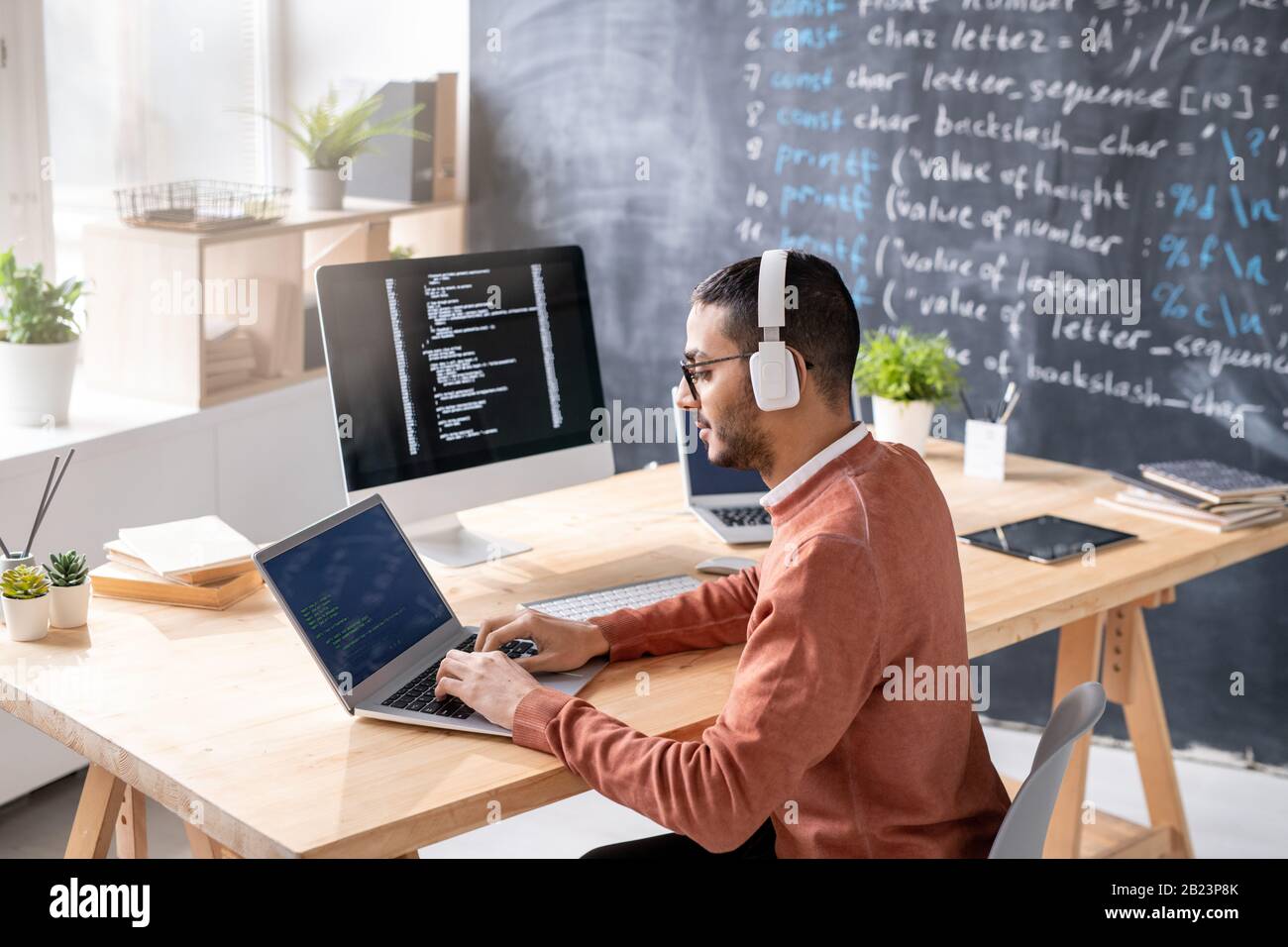 Busy young programmer with headphones analyzing data on laptop display ...