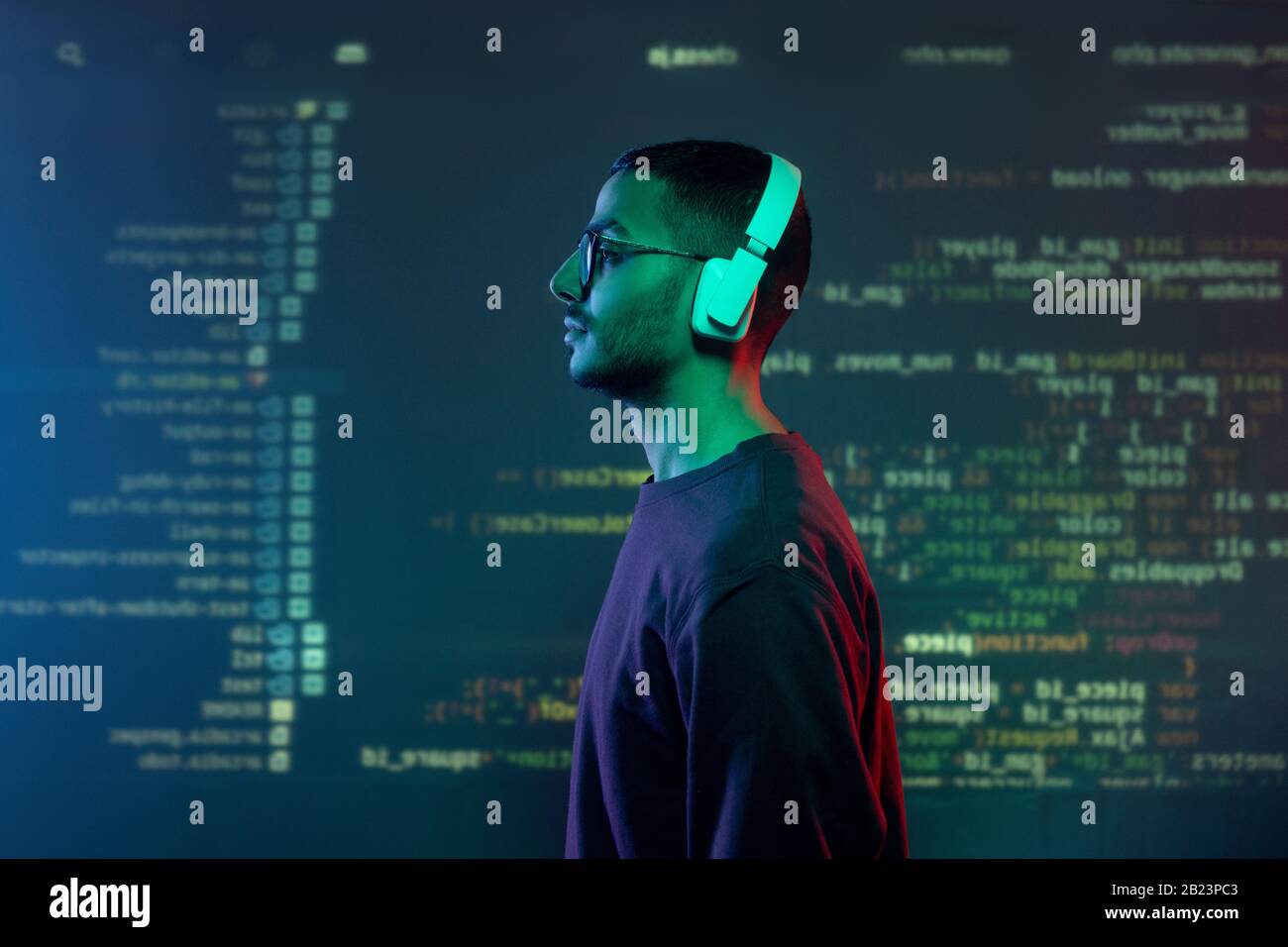 Side view of young programmer in headphones and casualwear standing ...