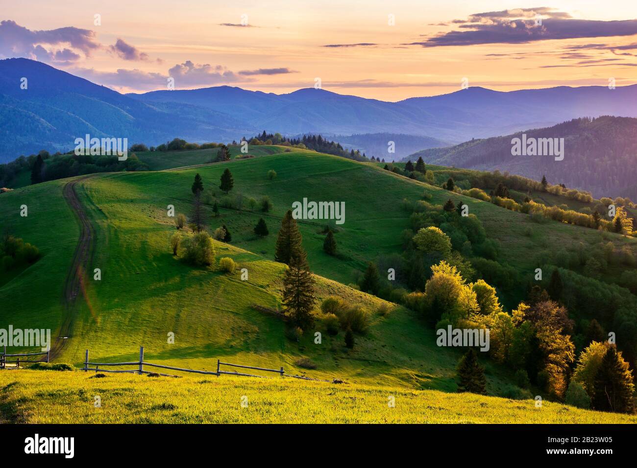 mountainous countryside in springtime at dusk. road, wooden fence and ...