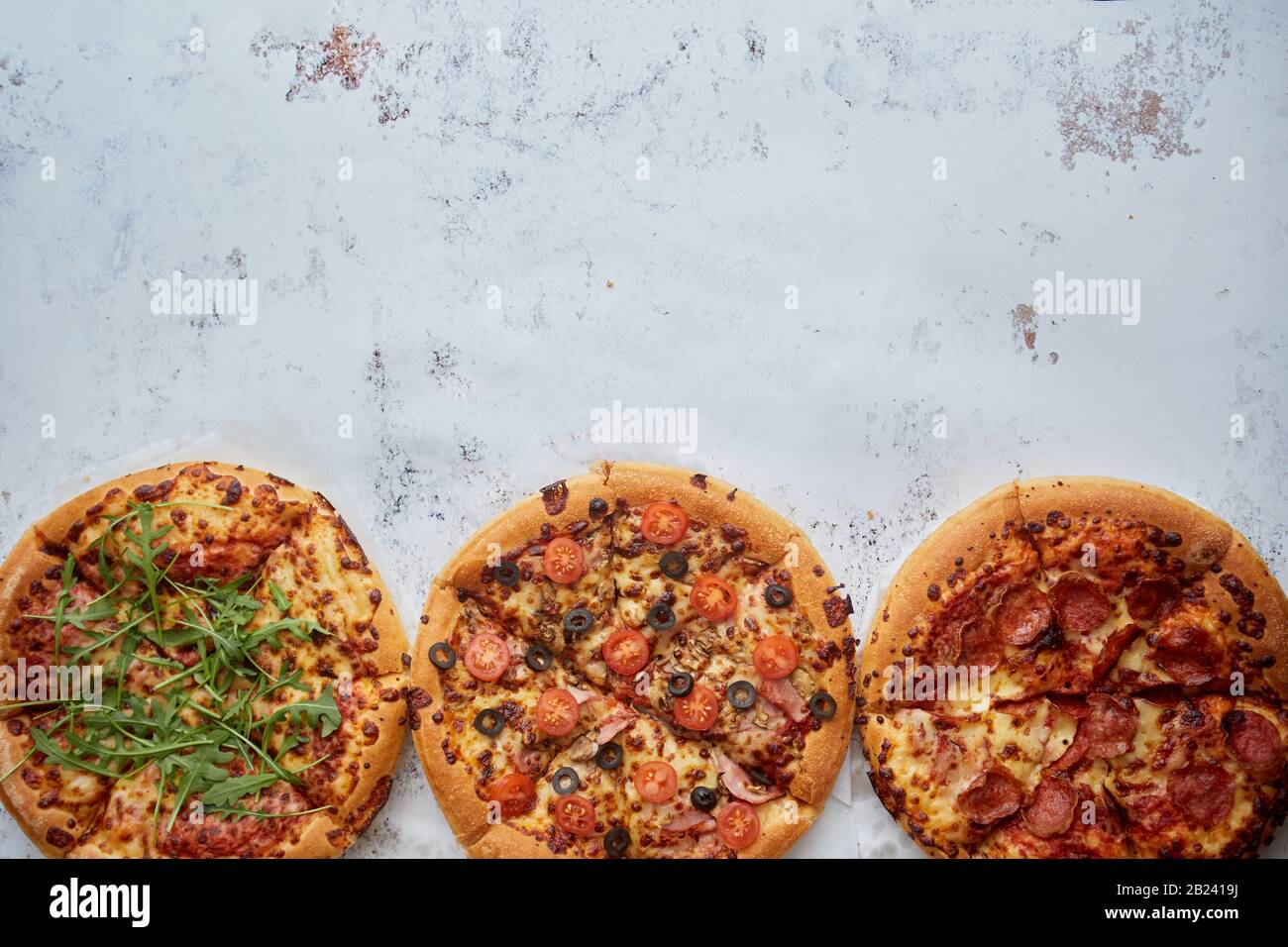 Three different kind of pizzas placed in a row on white rusty table ...