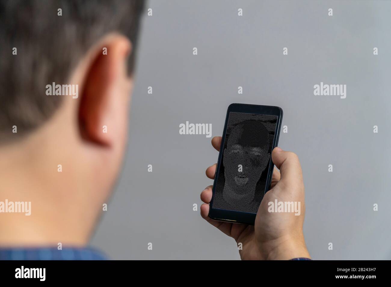 AI bot concept. A person looking at a smartphone screen with AI face on ...