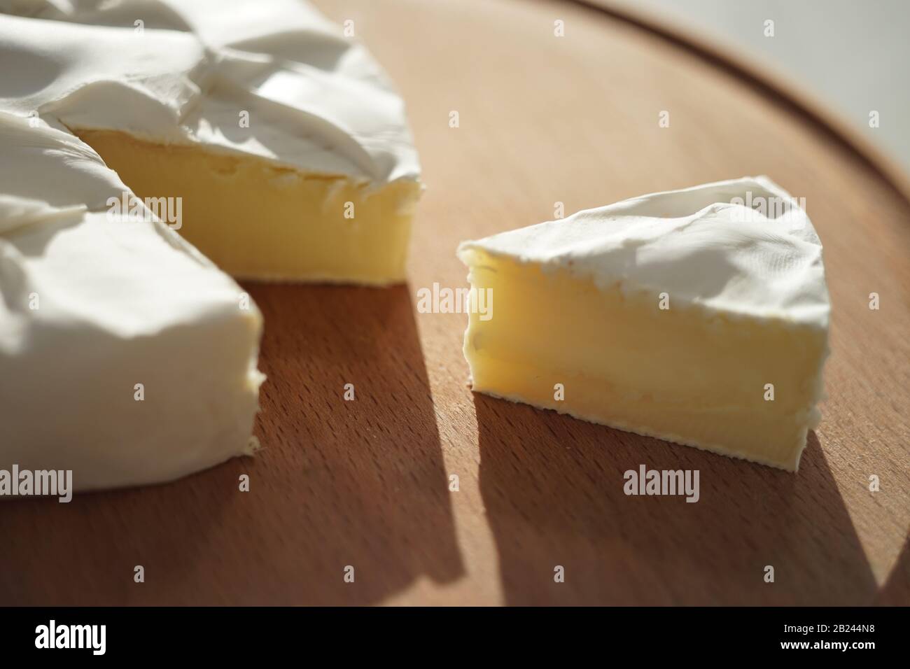 Camembert cheese slice and whole on a round wooden board. Side view ...