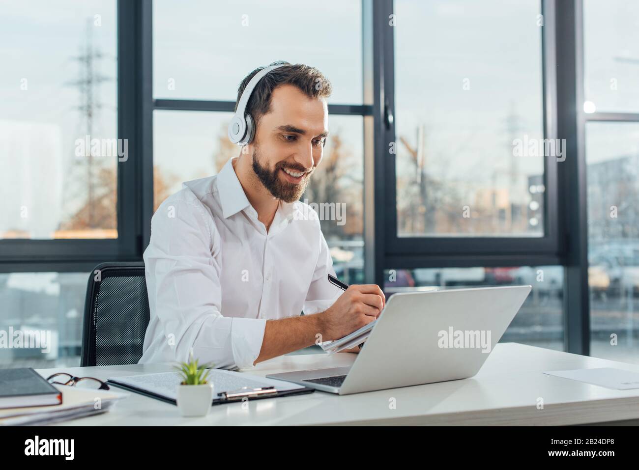 positive translator working online with headphones and laptop in office ...