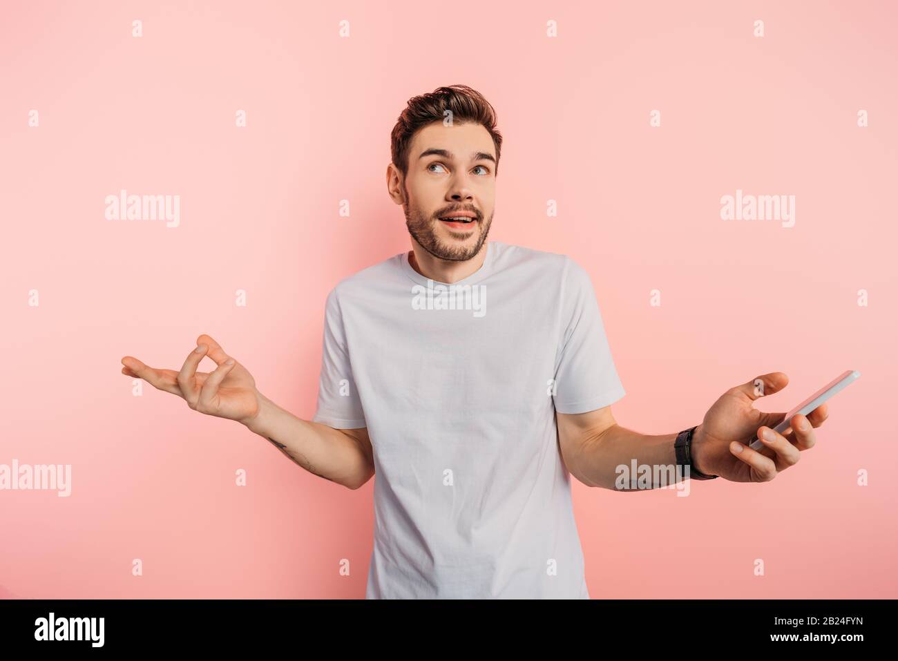 confused young man showing shrug gesture while holding smartphone on ...