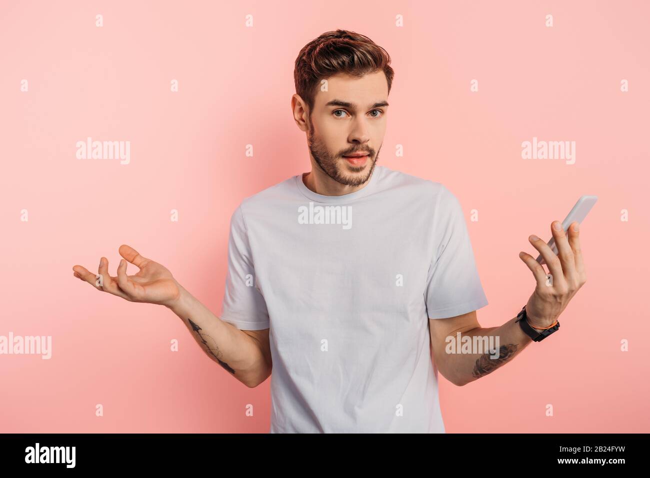 confused young man showing shrug gesture while holding smartphone on ...