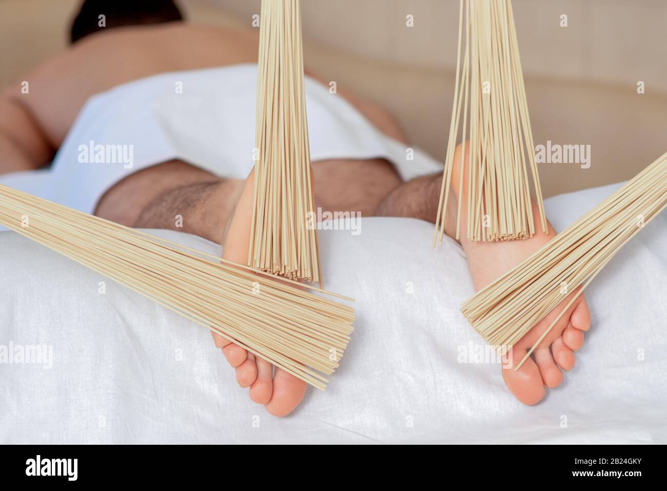 Close up of man receiving foot massage with bamboo brooms in four hands ...