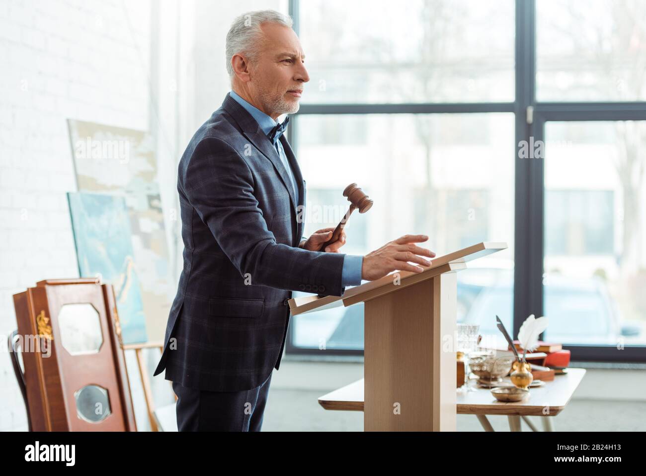 side view of auctioneer holding wooden gavel and looking away during ...