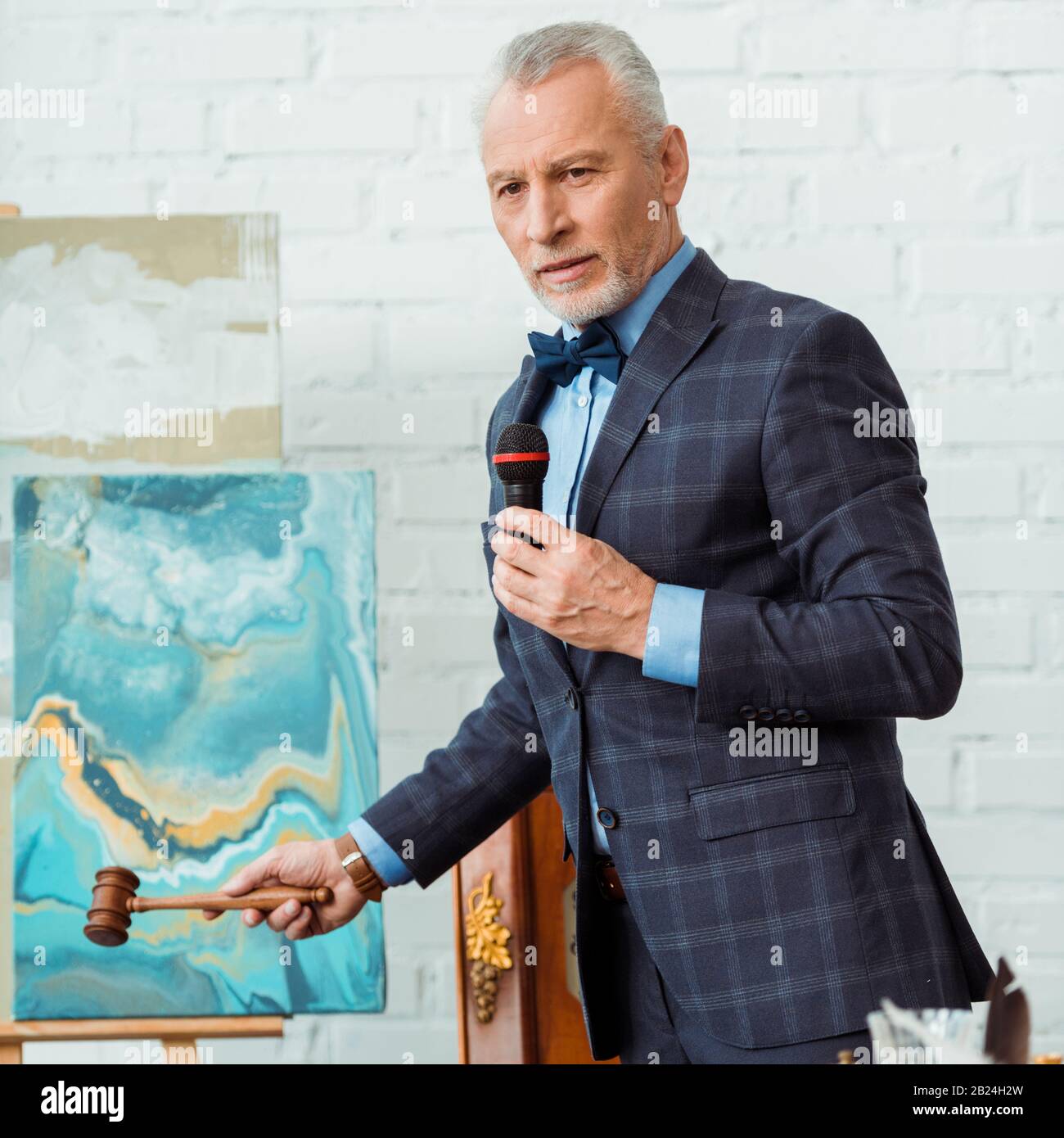 auctioneer in suit talking with microphone and holding gavel during ...
