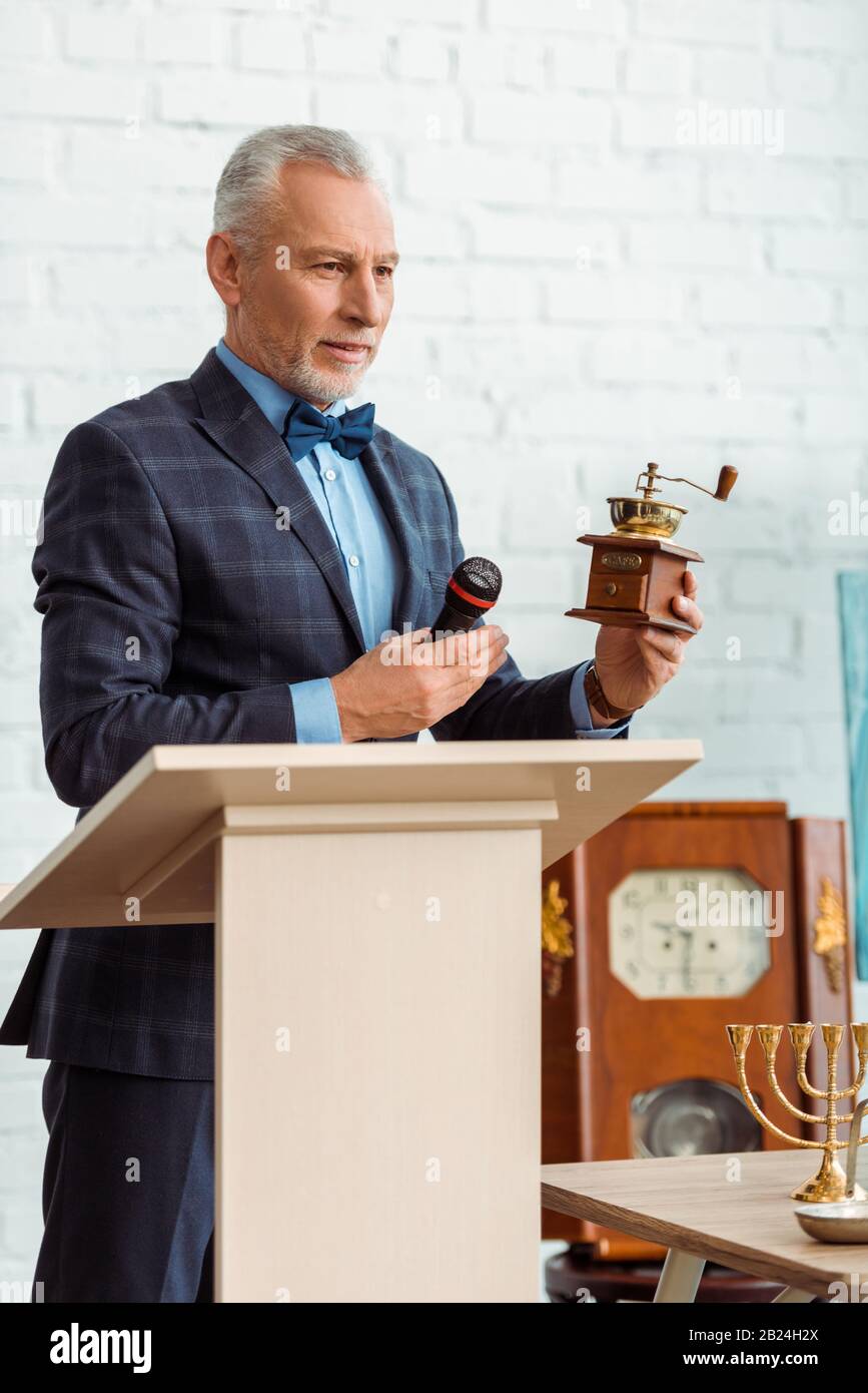 handsome auctioneer in suit pointing with hand at coffee grinder and ...