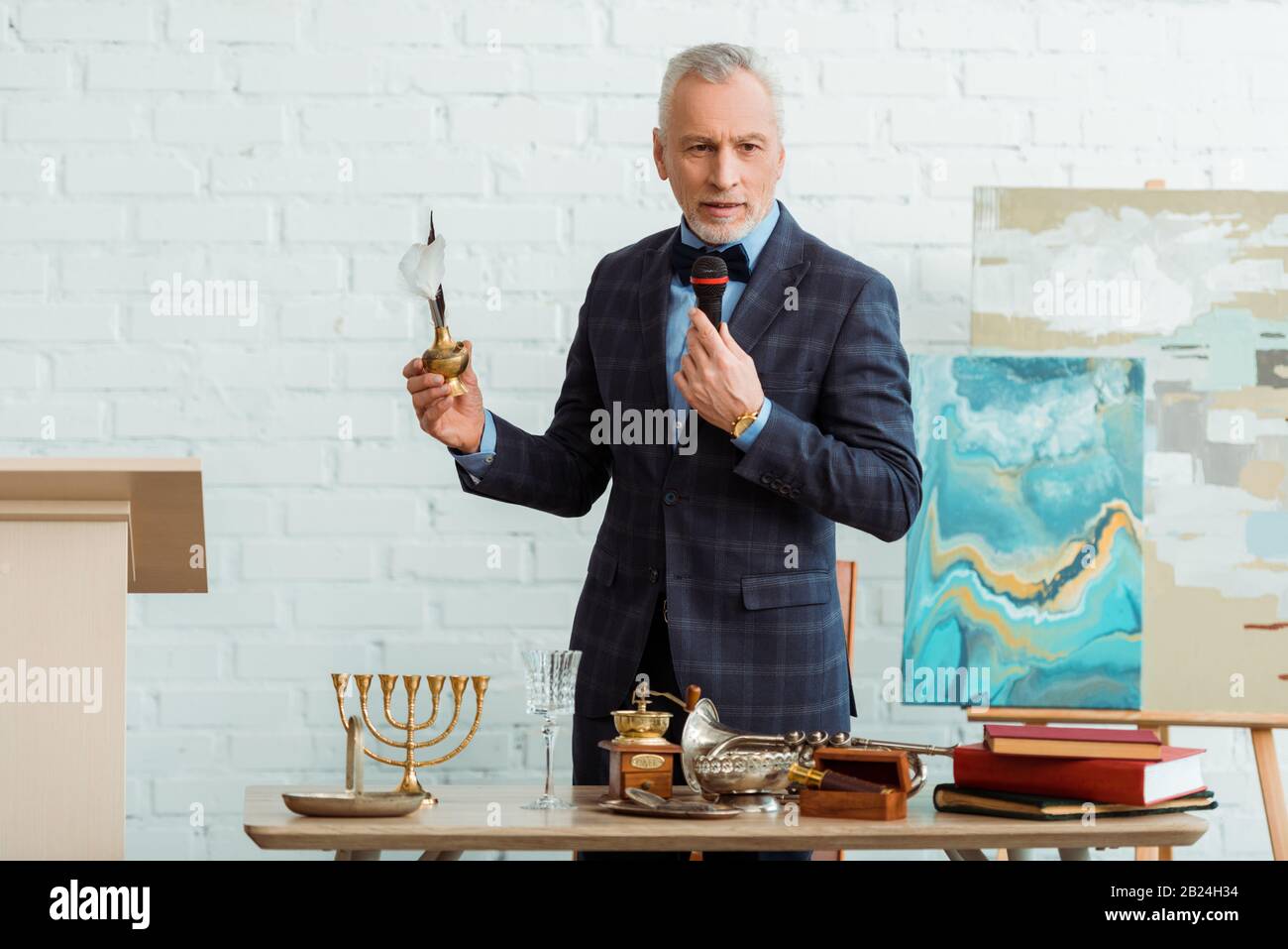 handsome auctioneer talking with microphone and holding feather pen ...