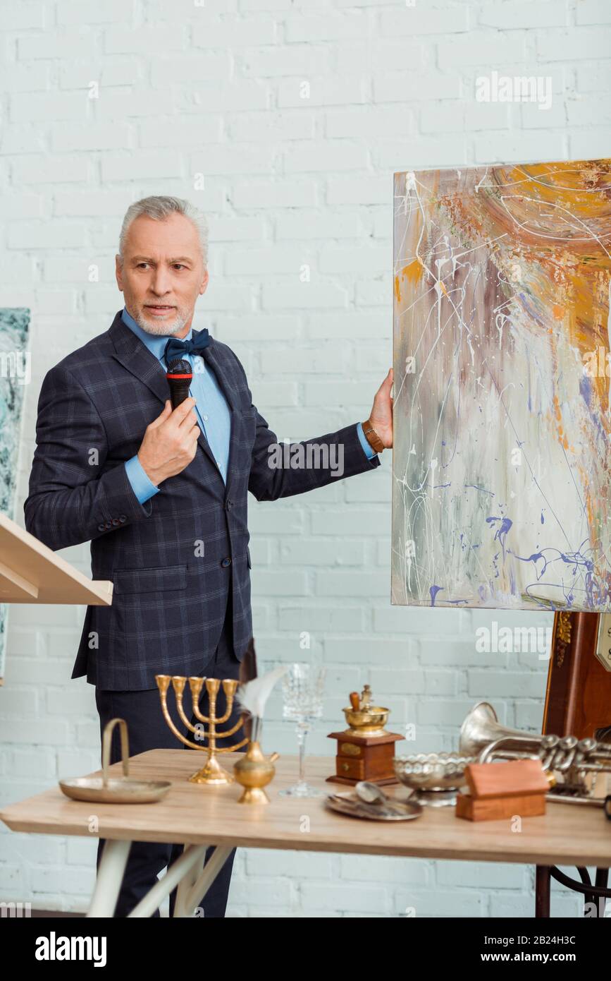 auctioneer talking with microphone and holding picture during auction ...