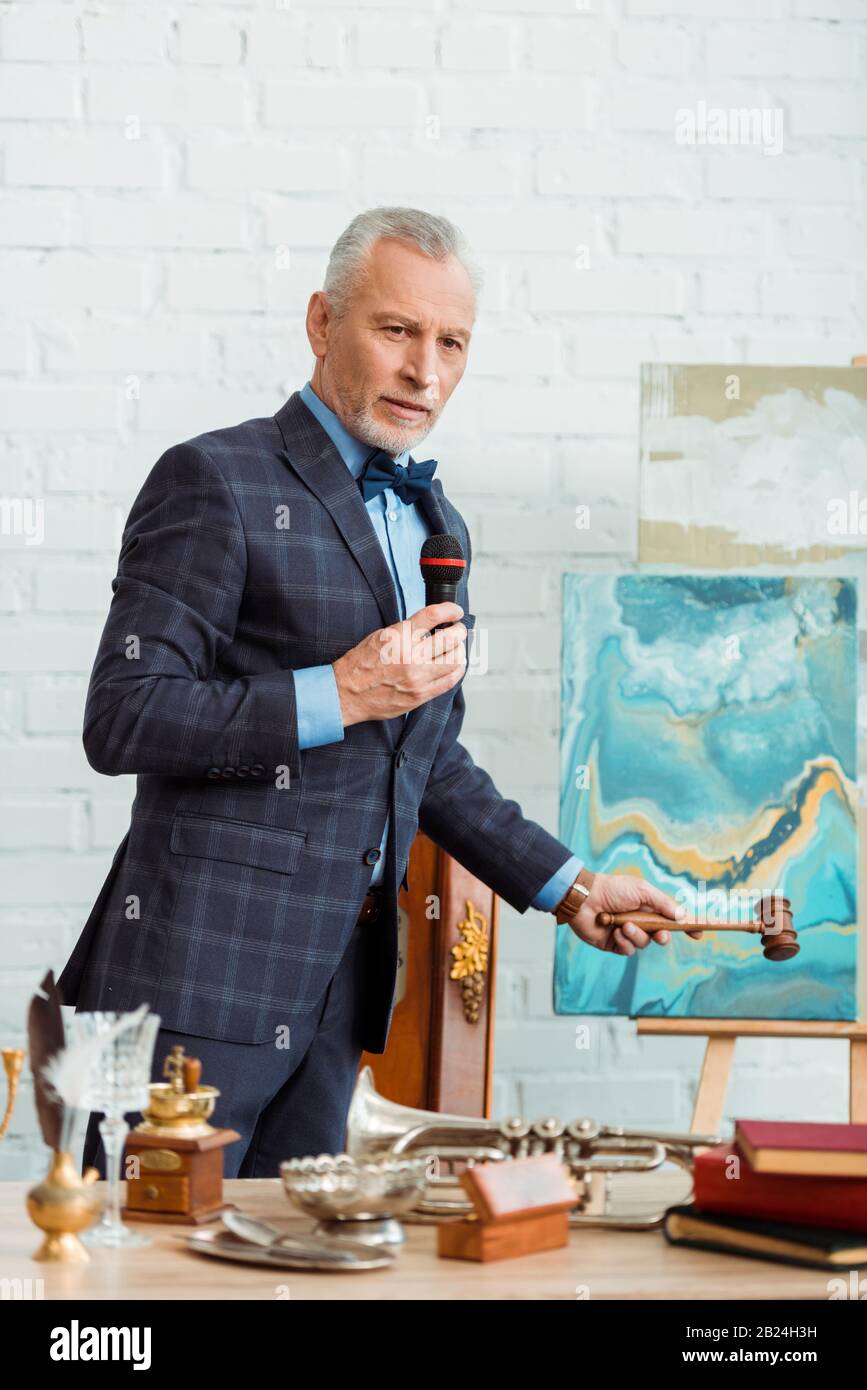 auctioneer in suit talking with microphone and holding gavel during ...