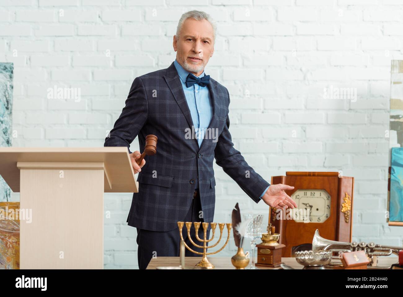 handsome auctioneer holding gavel and pointing with hand at antique ...