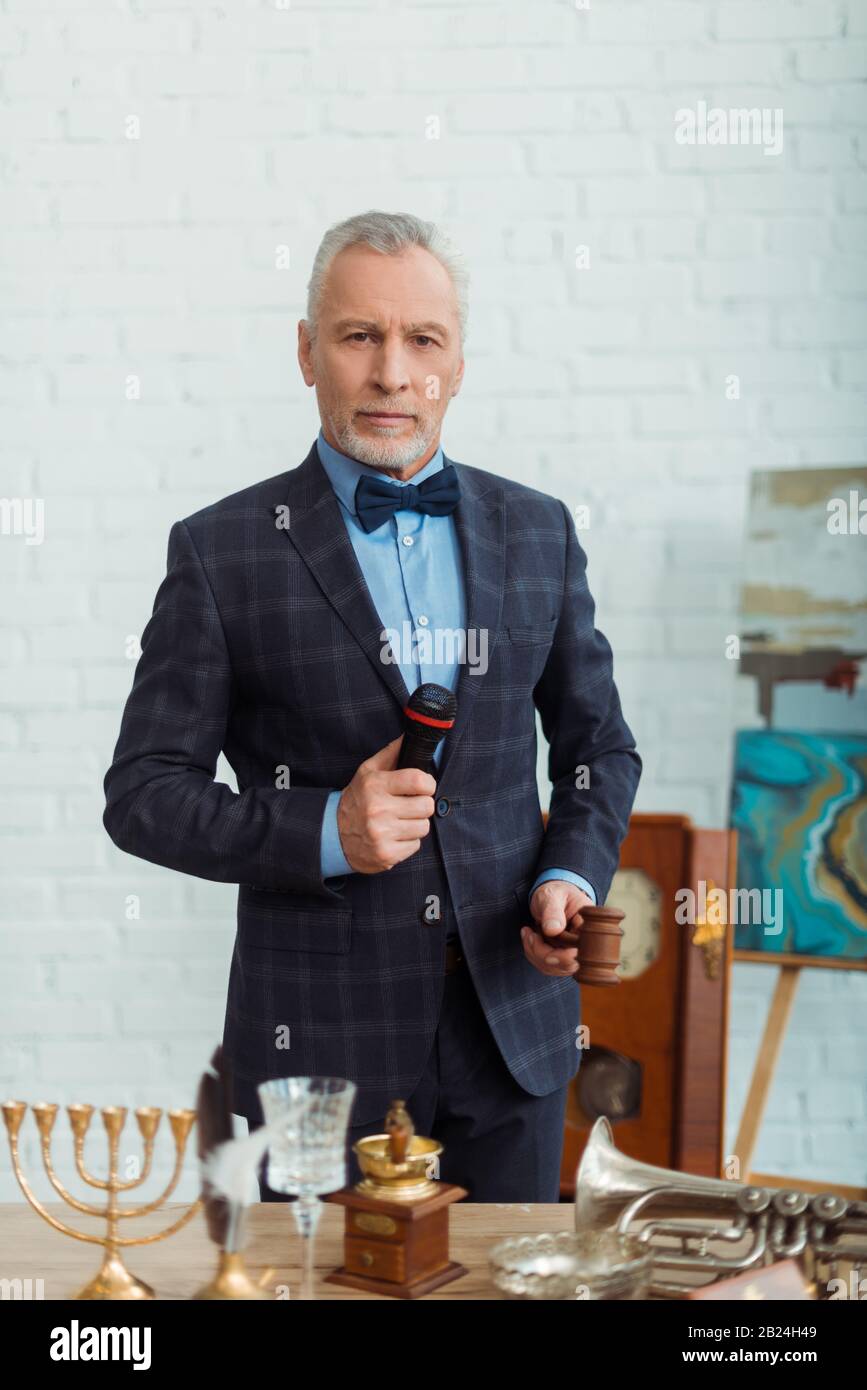 handsome auctioneer in suit holding microphone and gavel during auction ...
