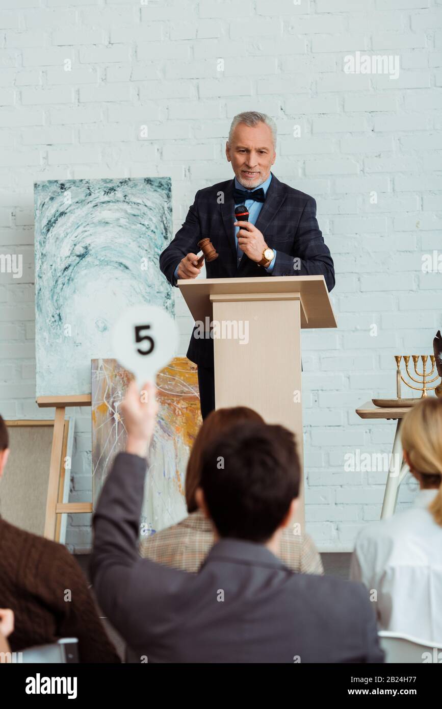 selective focus of smiling auctioneer talking with microphone and ...