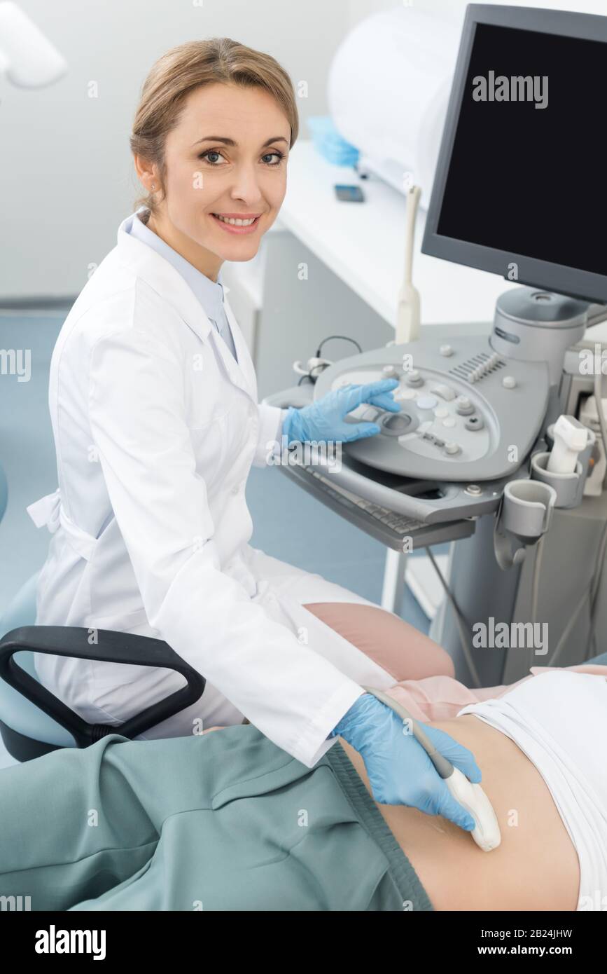Smiling Doctor Examining Stomach Of Female Patient With Ultrasound Scan
