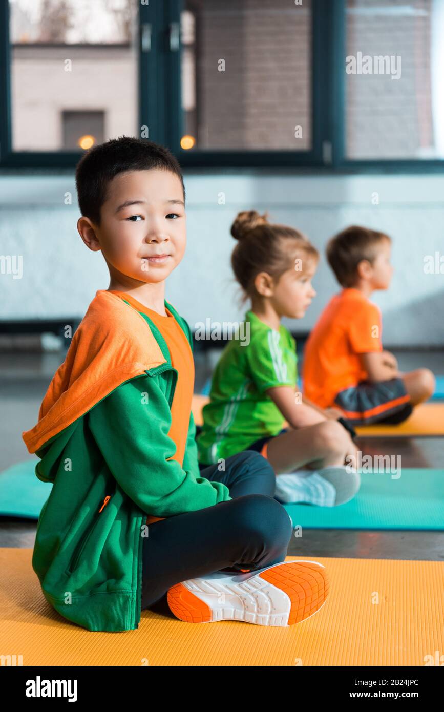 Selective focus of multicultural kids with crossed legs sitting on ...