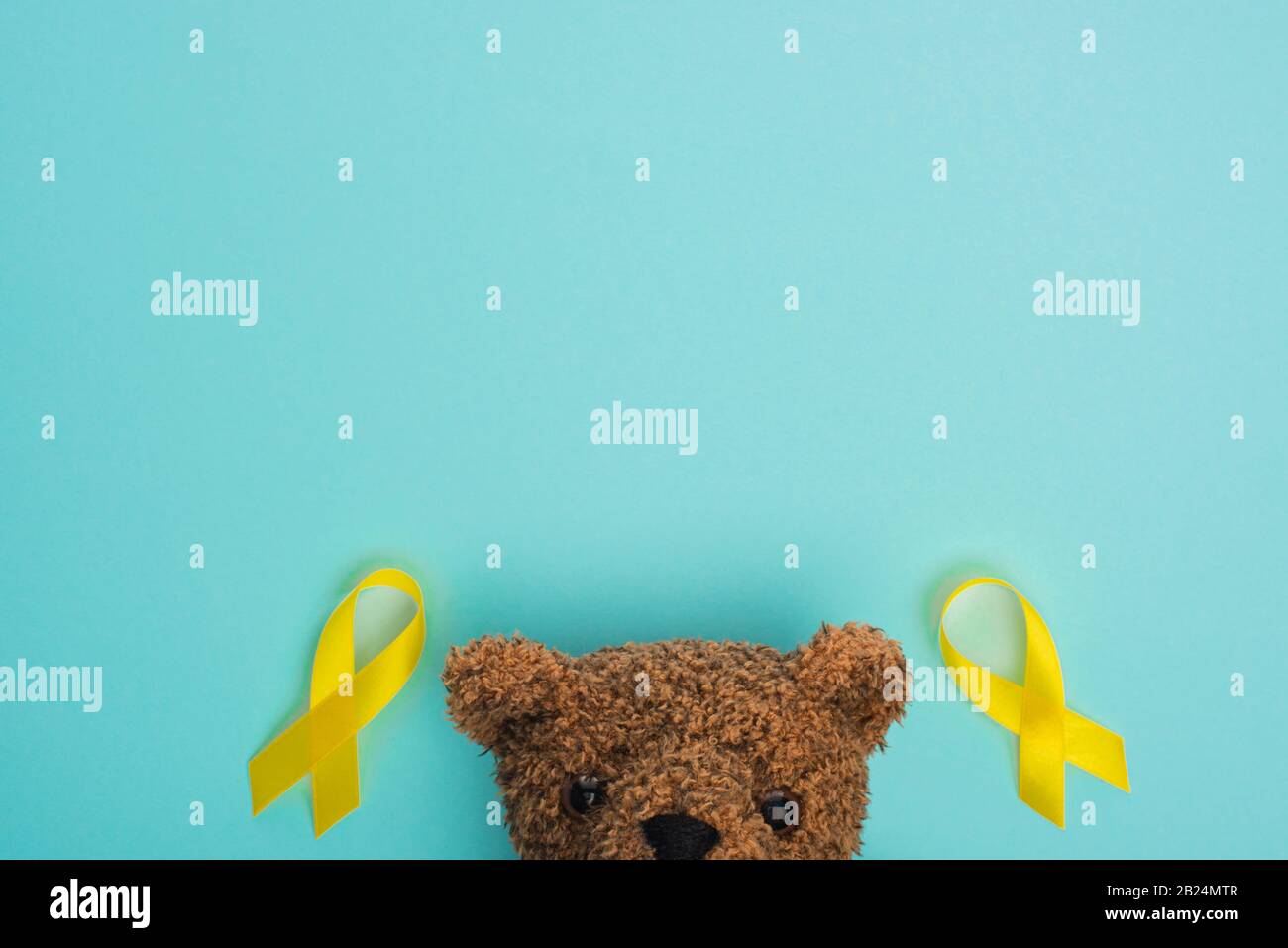 Top view of yellow awareness ribbons and brown teddy bear on blue ...