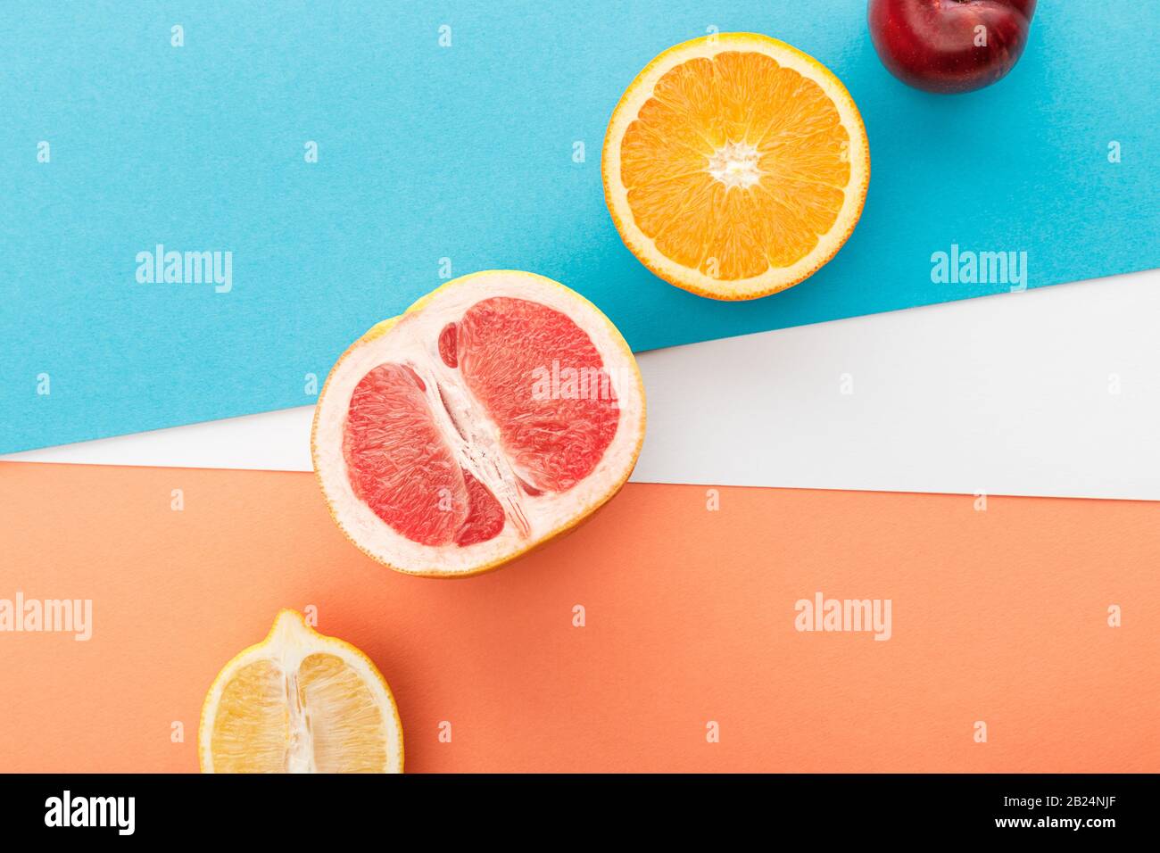 Top view of fruits halves and apple on blue, orange and white ...