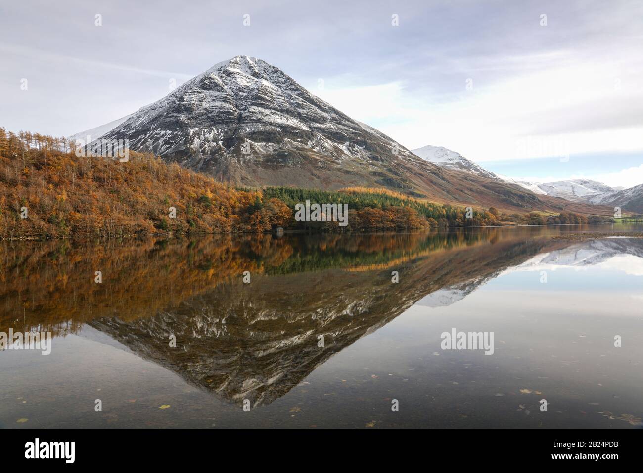Late autumnal reflections of woodland, Grasmoor fell and boathouse in ...