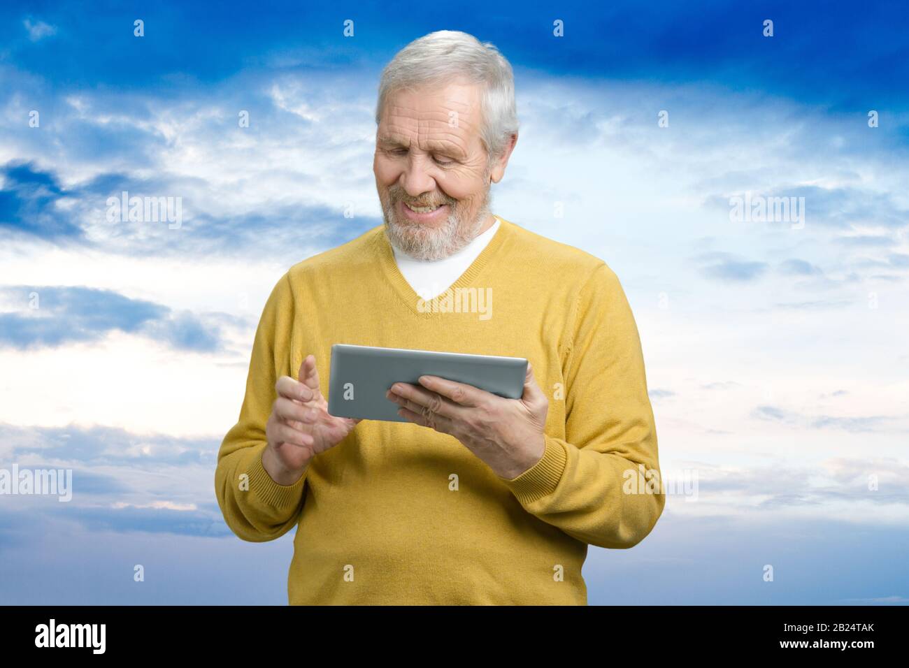 Old man with tablet over blue sky background Stock Photo - Alamy