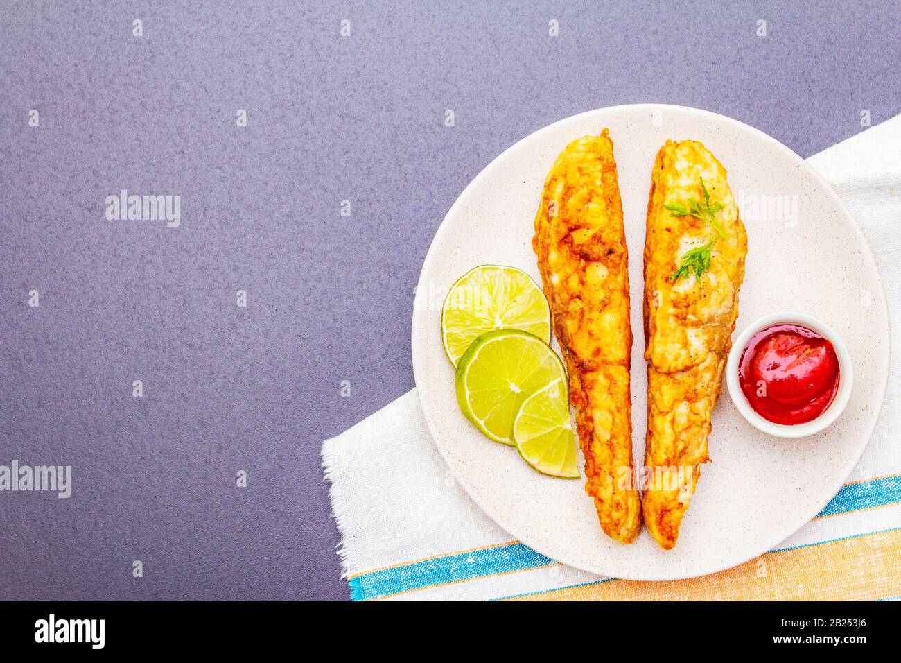 Grilled (fried) pollock in batter. On ceramic plate with lime, parsley ...