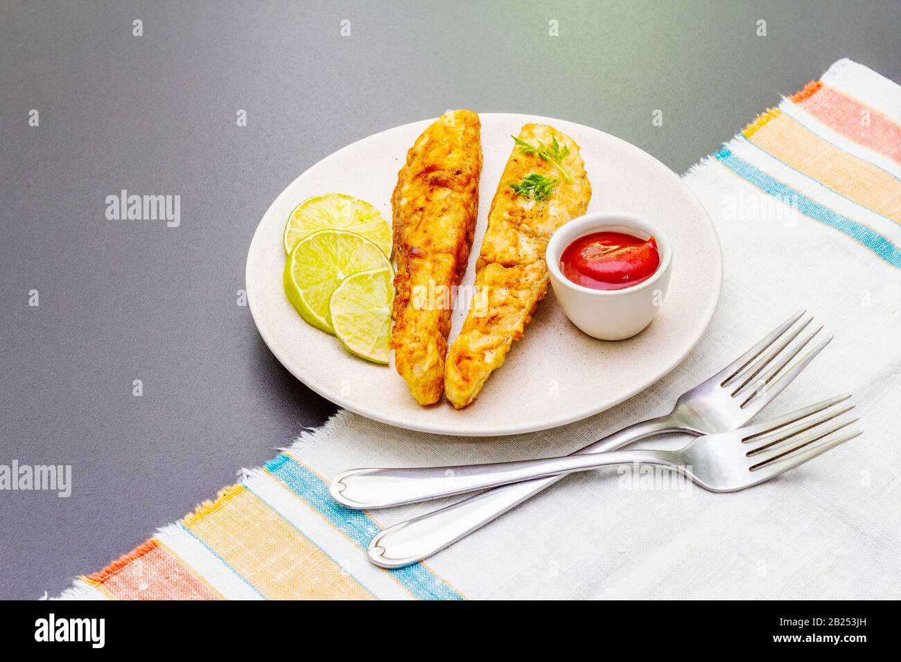 Grilled (fried) pollock in batter. On ceramic plate with lime, parsley ...