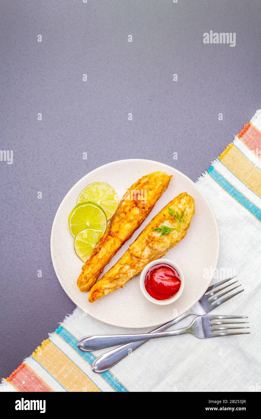 Grilled (fried) pollock in batter. On ceramic plate with lime, parsley ...