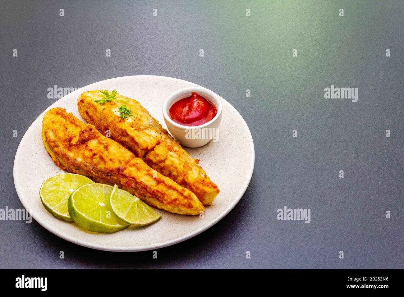 Grilled (fried) pollock in batter. On ceramic plate with lime, parsley ...