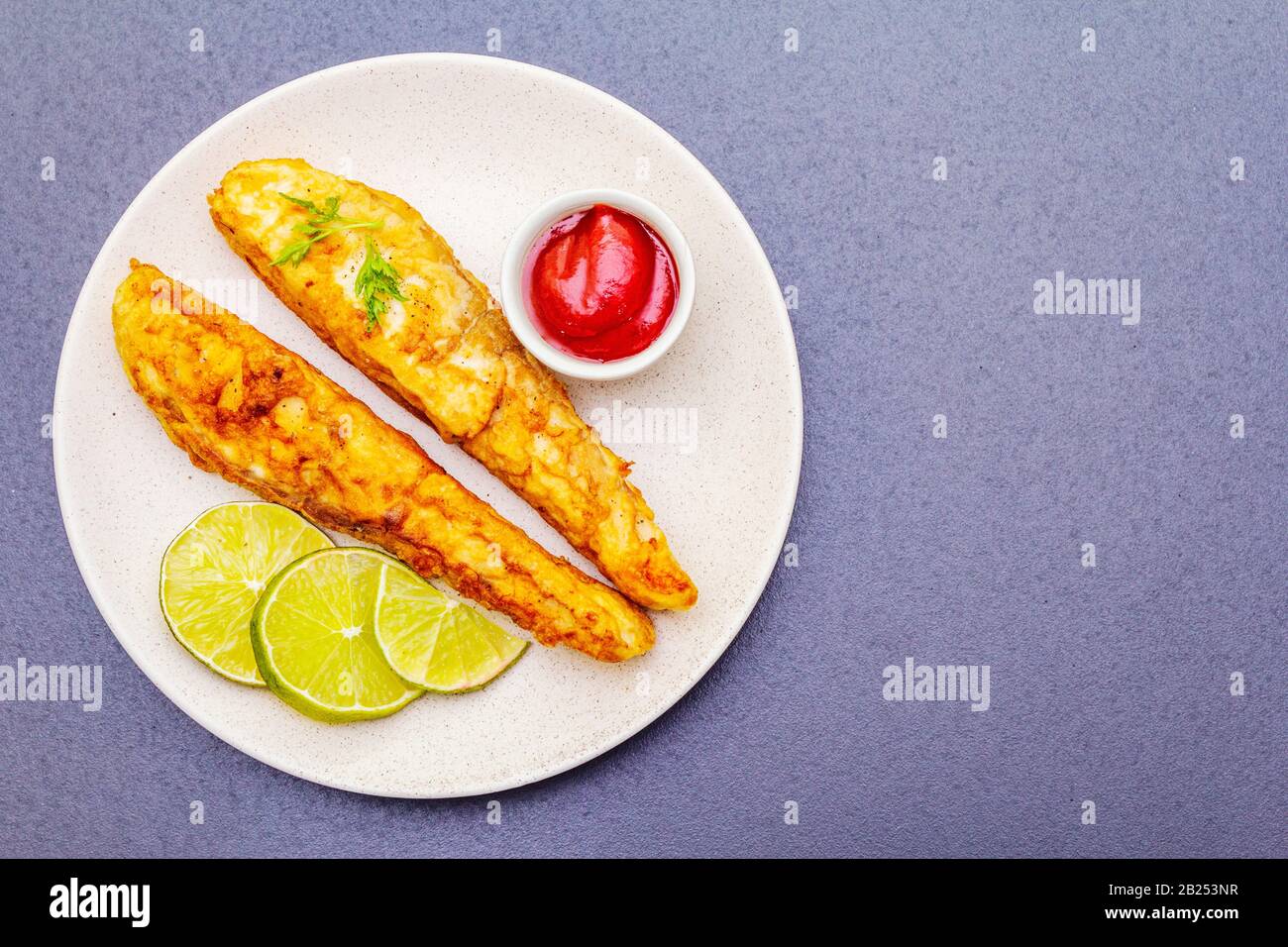 Grilled (fried) pollock in batter. On ceramic plate with lime, parsley ...