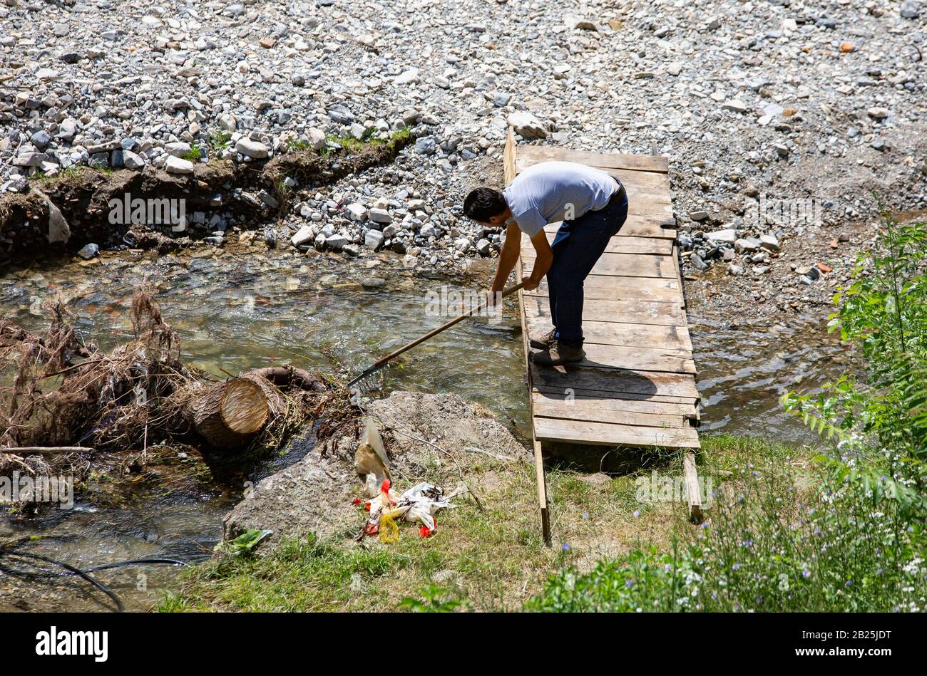 Man cleaning a stream, collecting garbage, litter from a brook ...