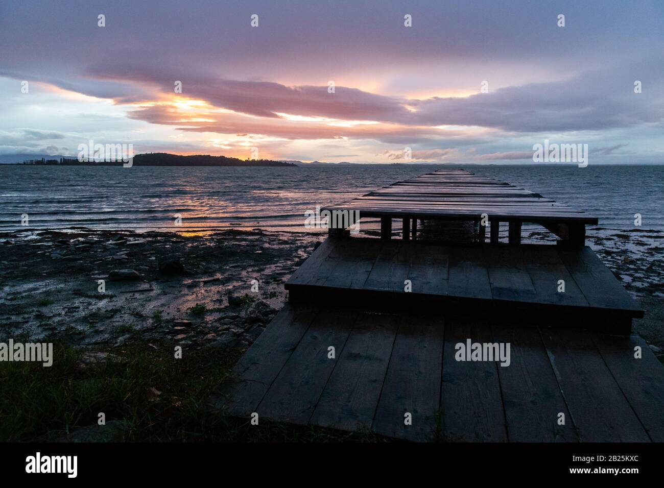 Low point view of a pier on a lake with a ray of sun against a moody ...