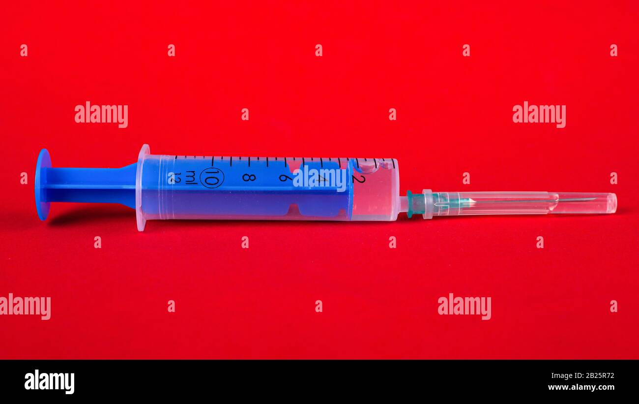 medical blue syringe on a red background close up Stock Photo - Alamy