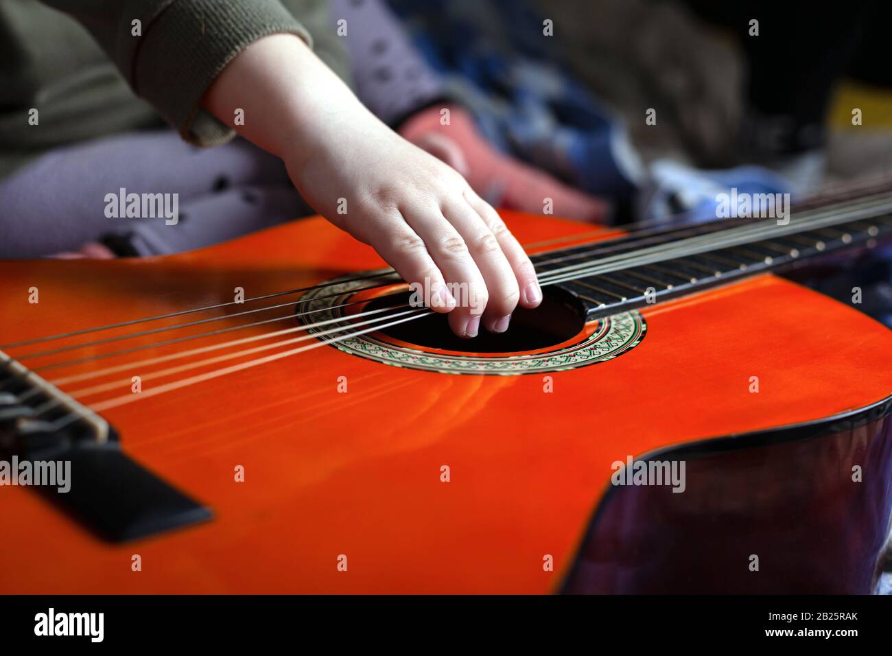 children's hand pulls the strings on an orange acoustic guitar Stock ...