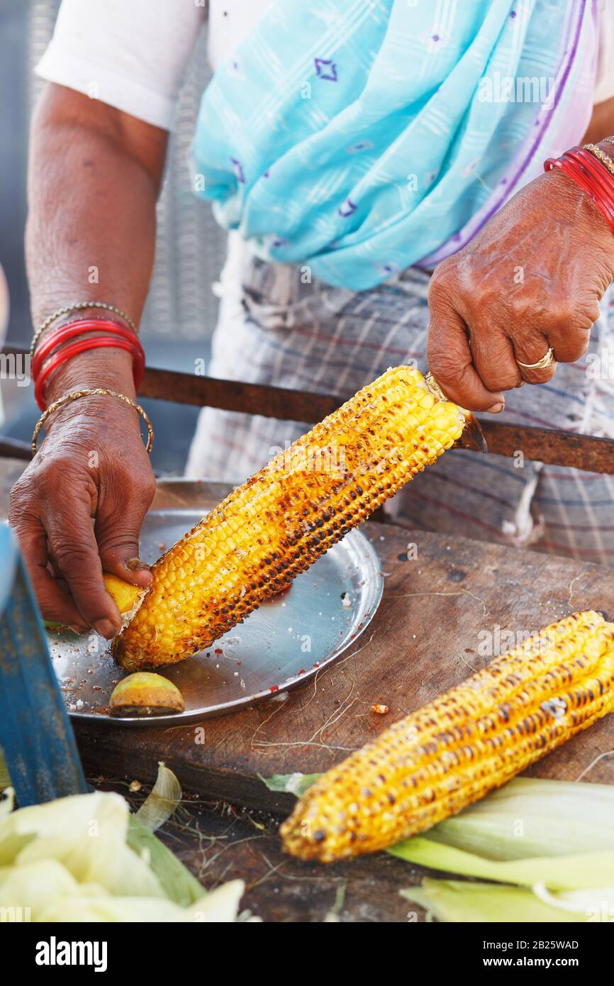 Close-up hands of female street vendor is rubbing a roasted sweet corn ...
