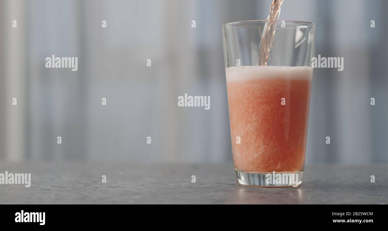 pour orange fizzy drink into pint glass on concrete countertop with ...