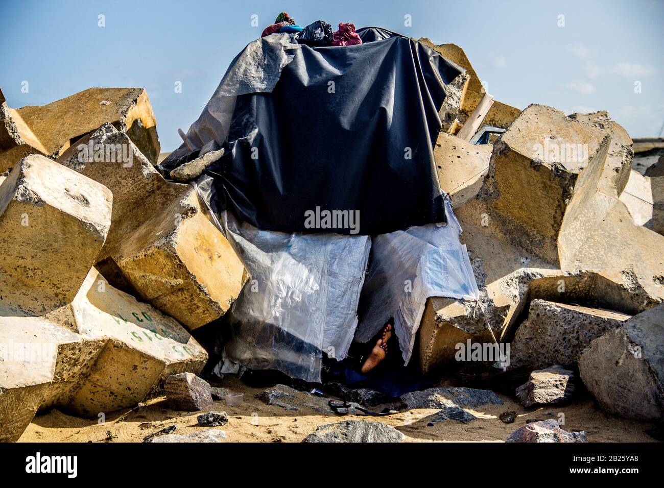 A homeless man legs peeks out under the sheets on a street in Lagos ...