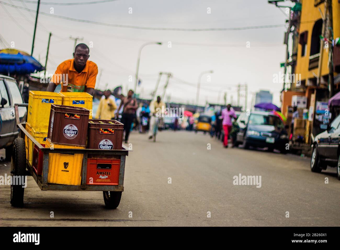 A man push a wheel-barrow filled with beer crates on a street in Lagos ...