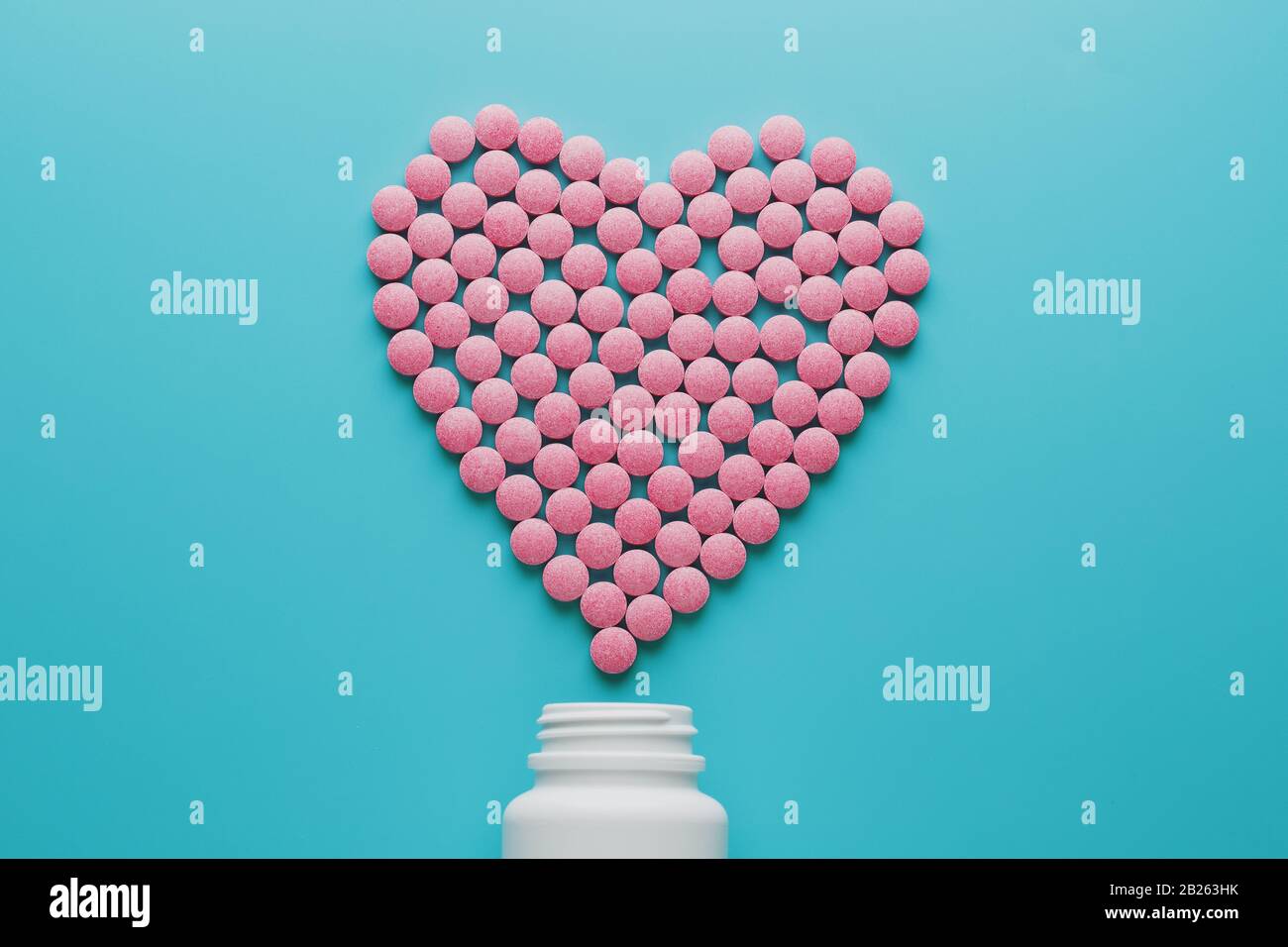 Pink B12 pills in the shape of a heart on a blue background, poured out ...