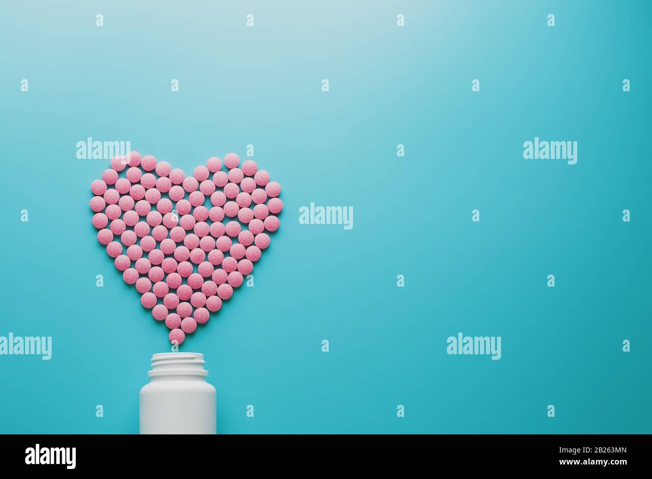 Pink B12 pills in the shape of a heart on a blue background, poured out ...