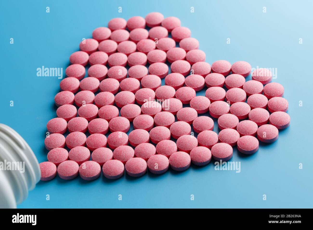 Pink B12 pills in the shape of a heart on a blue background, poured out ...