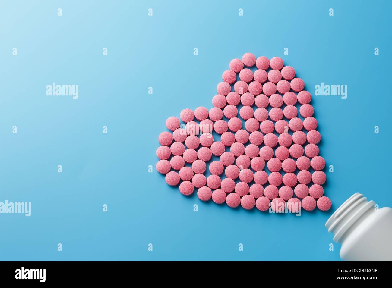 Pink B12 pills in the shape of a heart on a blue background, poured out ...
